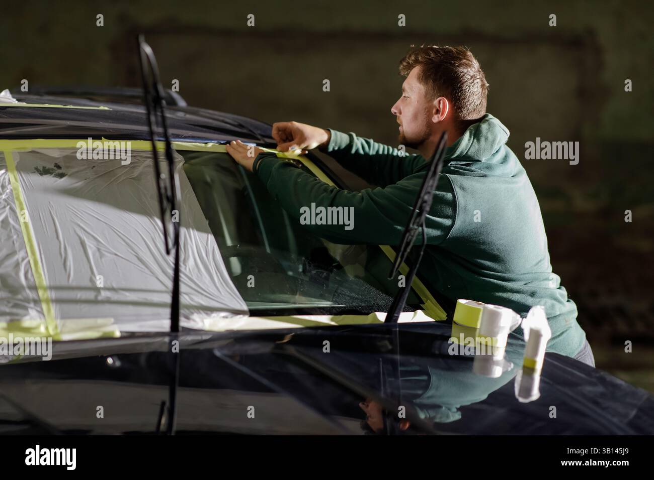A car detailing professional is focused on taping areas of a vehicle ...