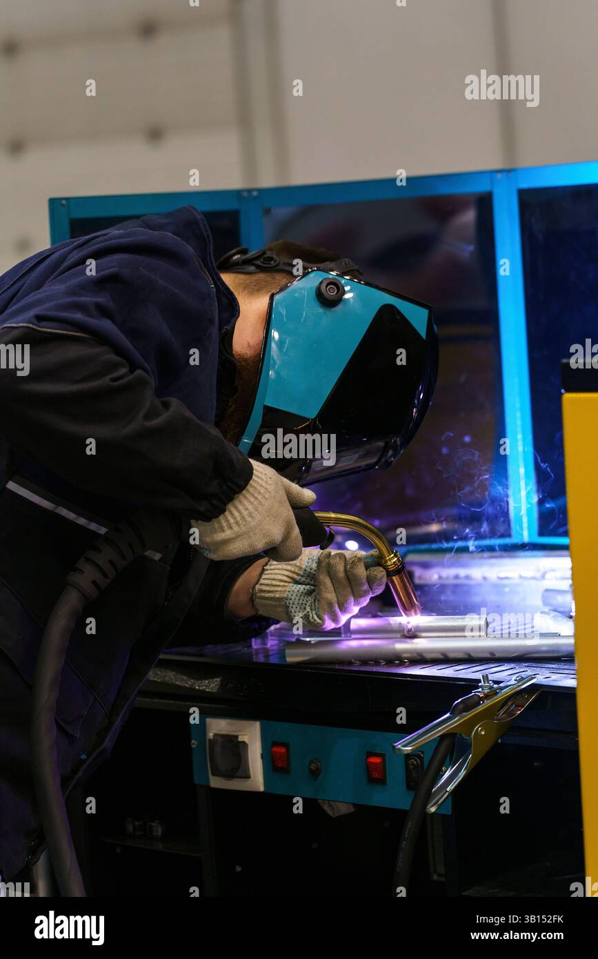 a male welder at the workplace welds parts, sparks from welding, welder ...