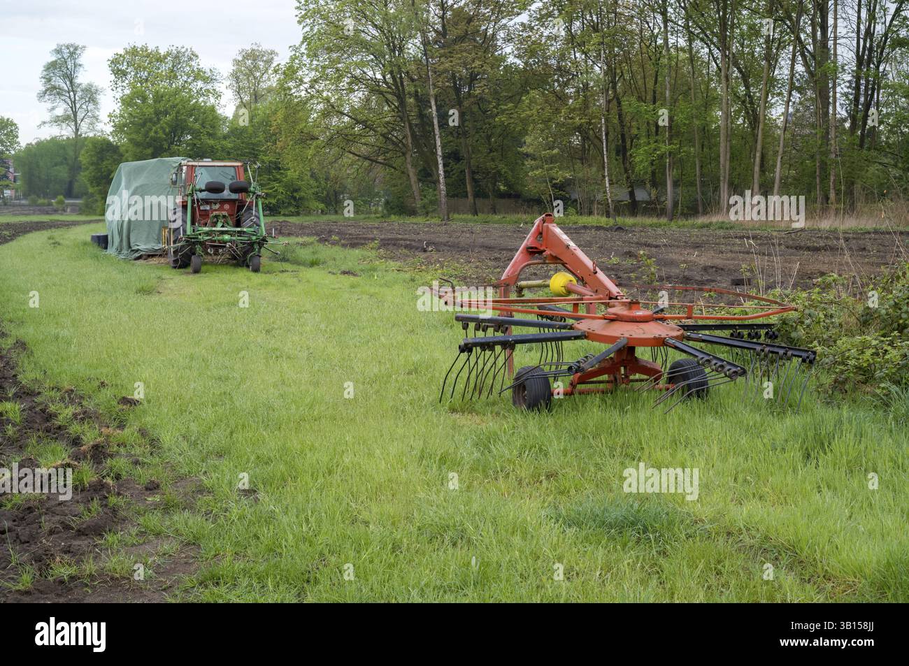 Red rotary rake and green tractor with baler parked in a field, ready ...