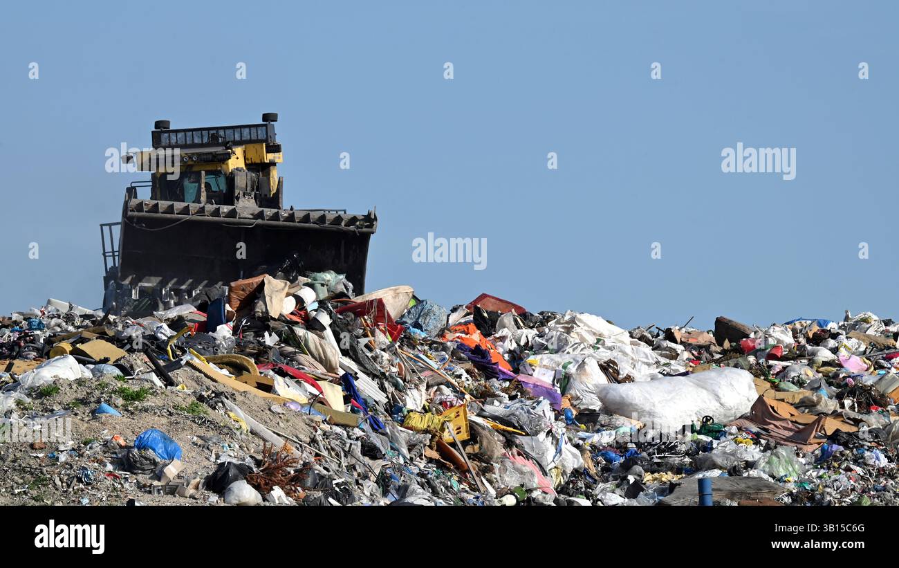 Industrial compactor operating on a pile of waste in a landfill site ...