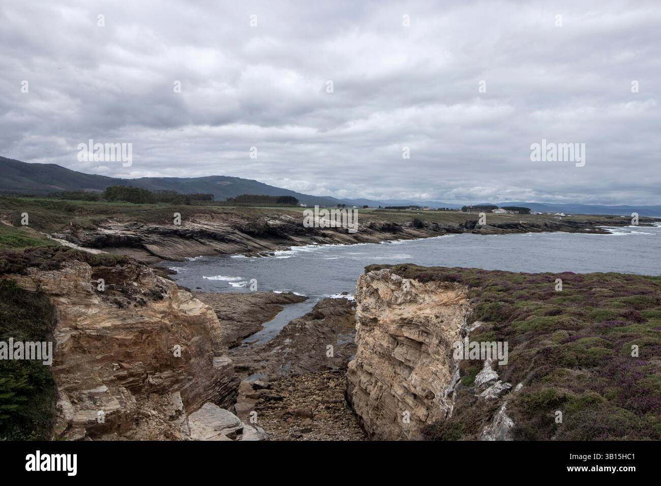 Rocky cliffs meet the ocean waves under a dramatic cloudy sky, creating ...