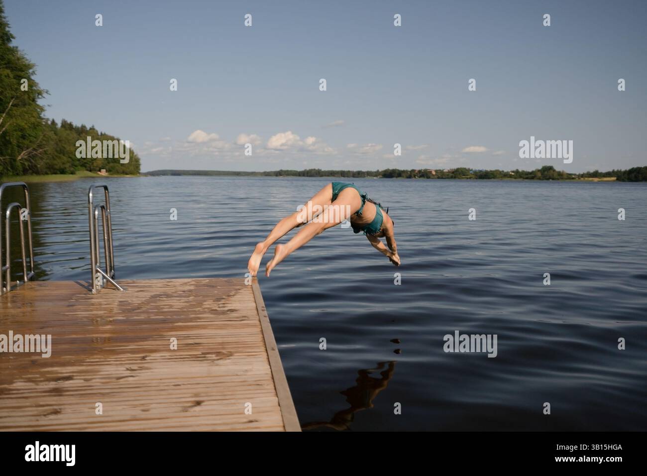 Woman in a swimsuit jumping headfirst from a pier into a lake. Capturing a powerful dive in ...
