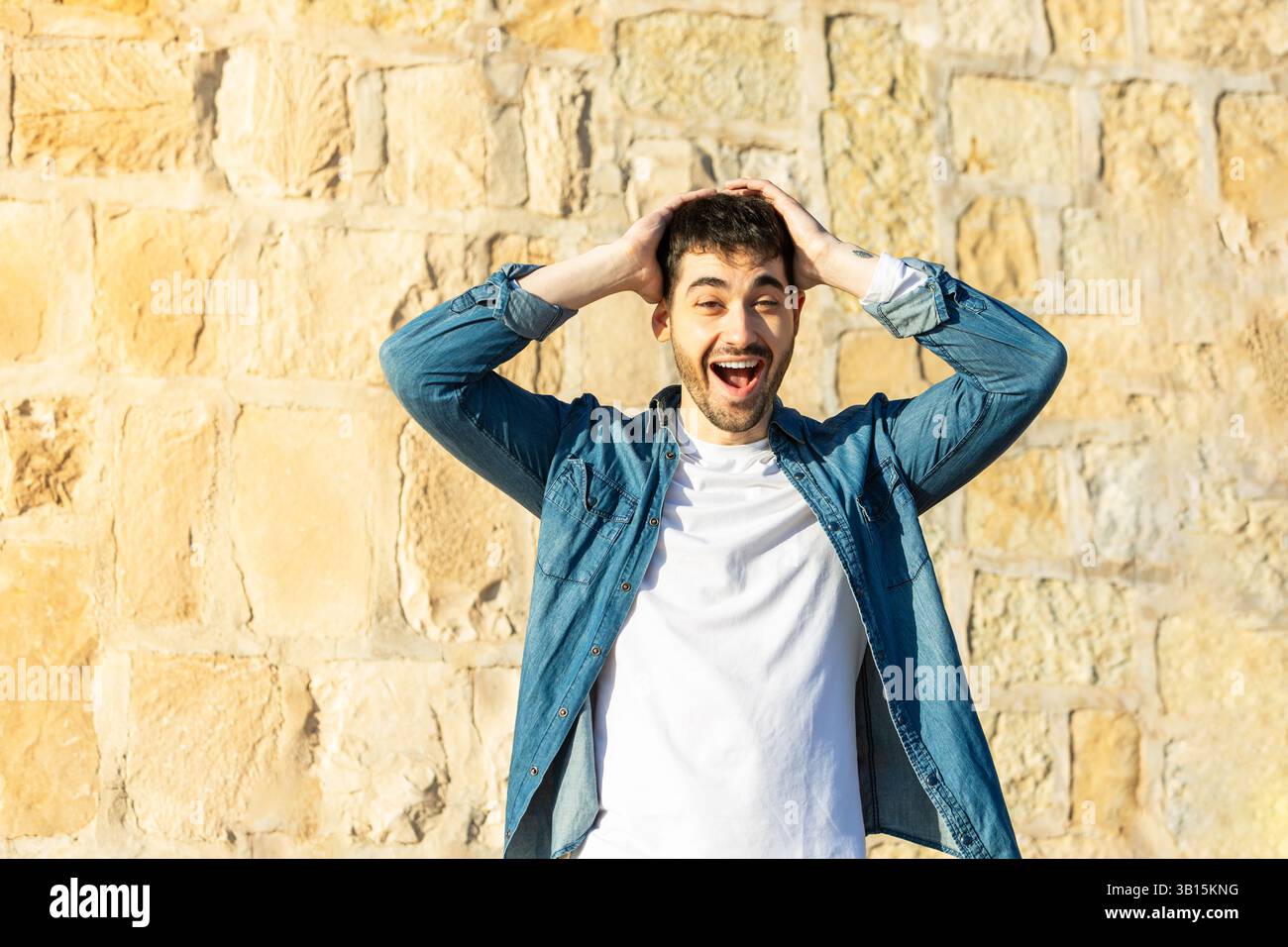 Young man in denim shirt and white t-shirt expressing excitement and ...