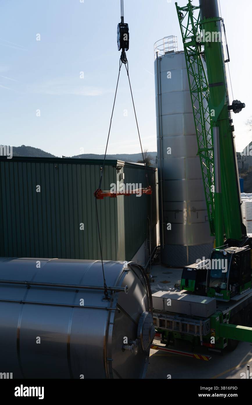 An industrial crane lifting a large stainless steel tank outside a ...