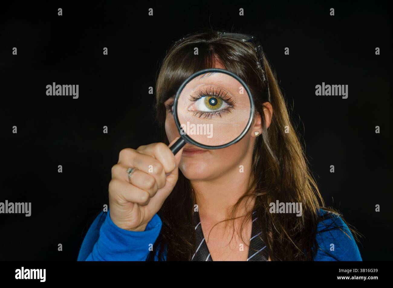 Young sleuth detective female holding a magnifying glass to her eye to ...