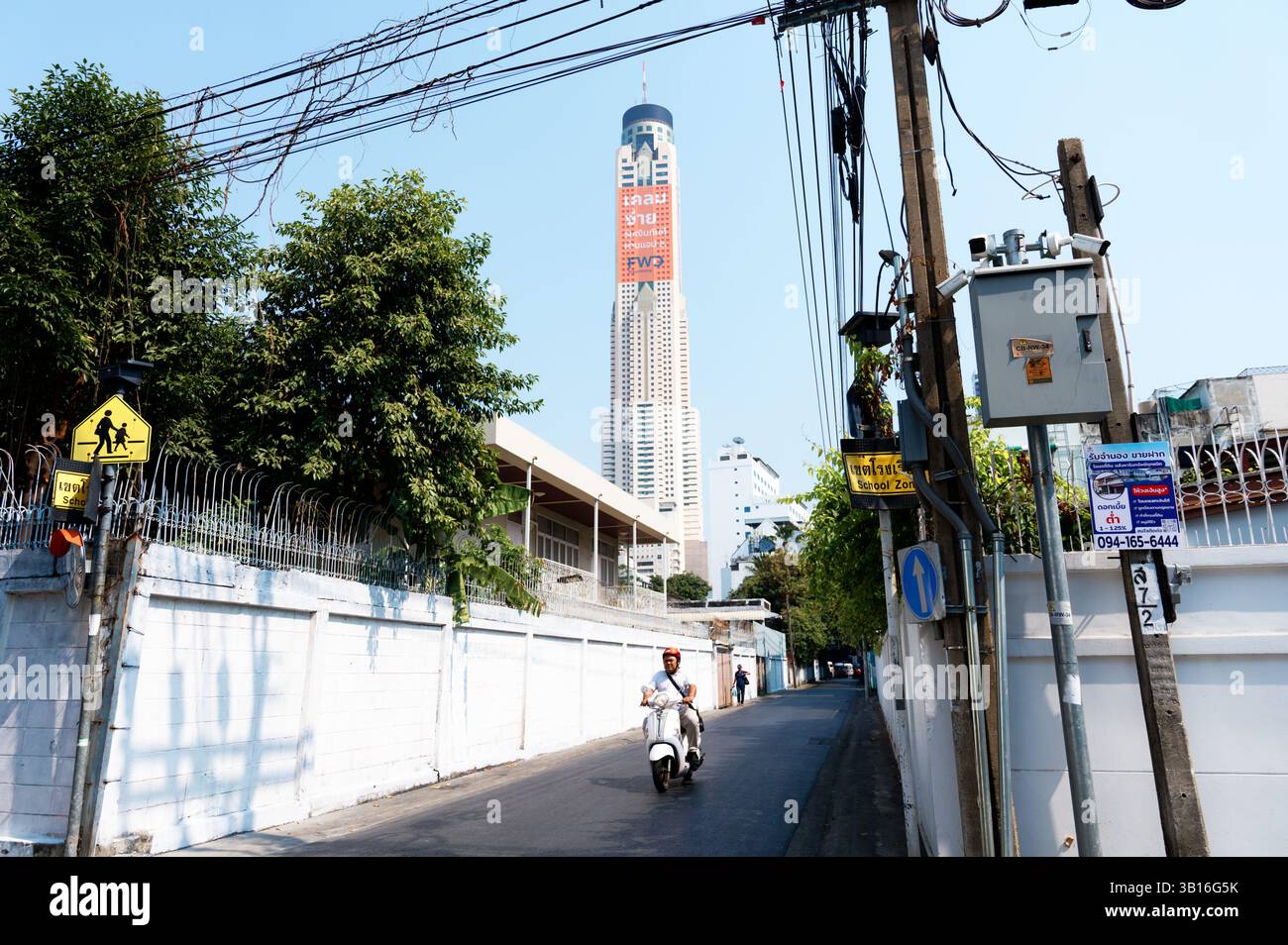 Scooter rides down a quiet alleyway with Baiyoke Tower II rising in the backdrop Stock Photo - Alamy