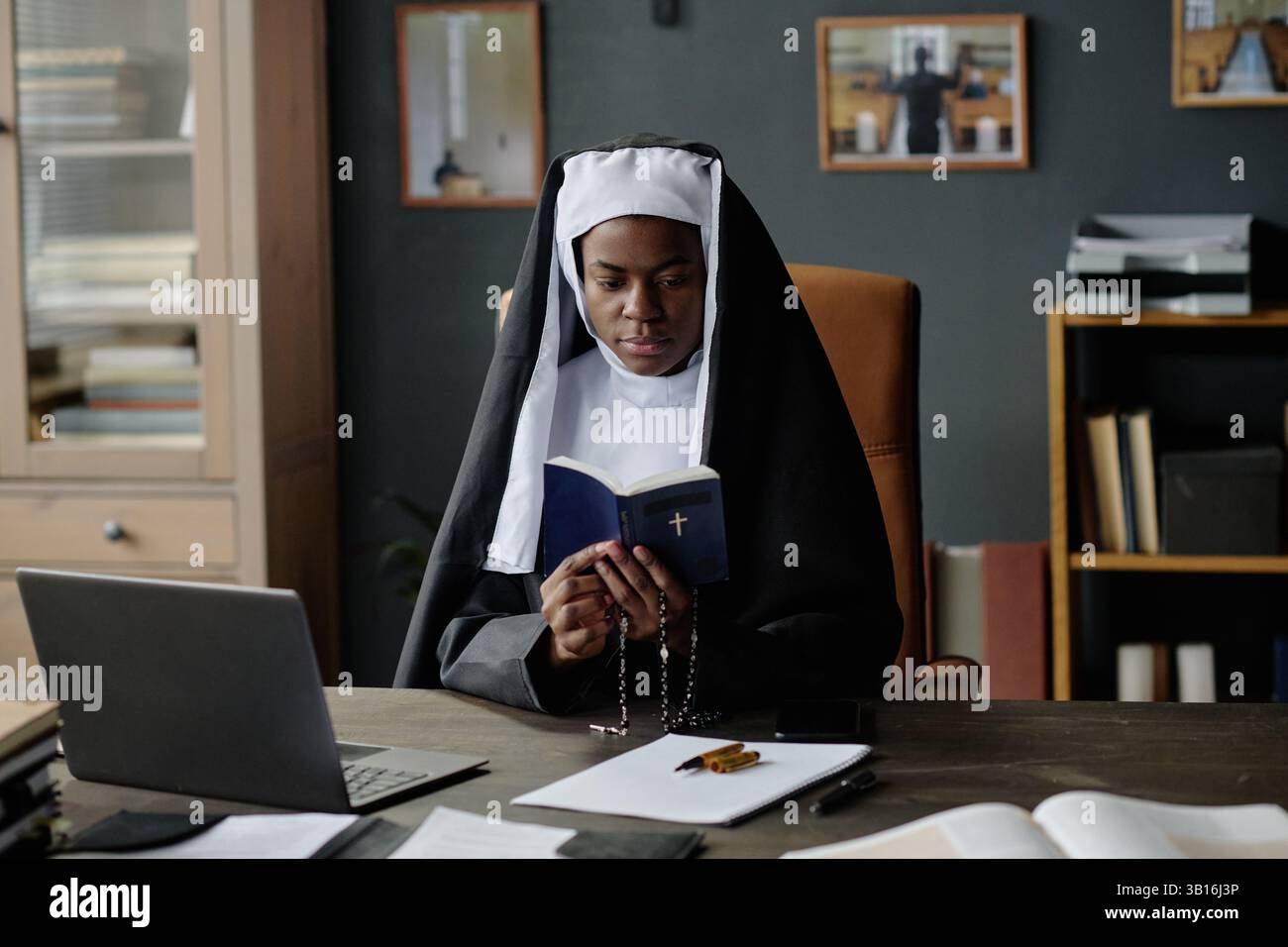 Young African American nun dressed in black habit reading carefully ...