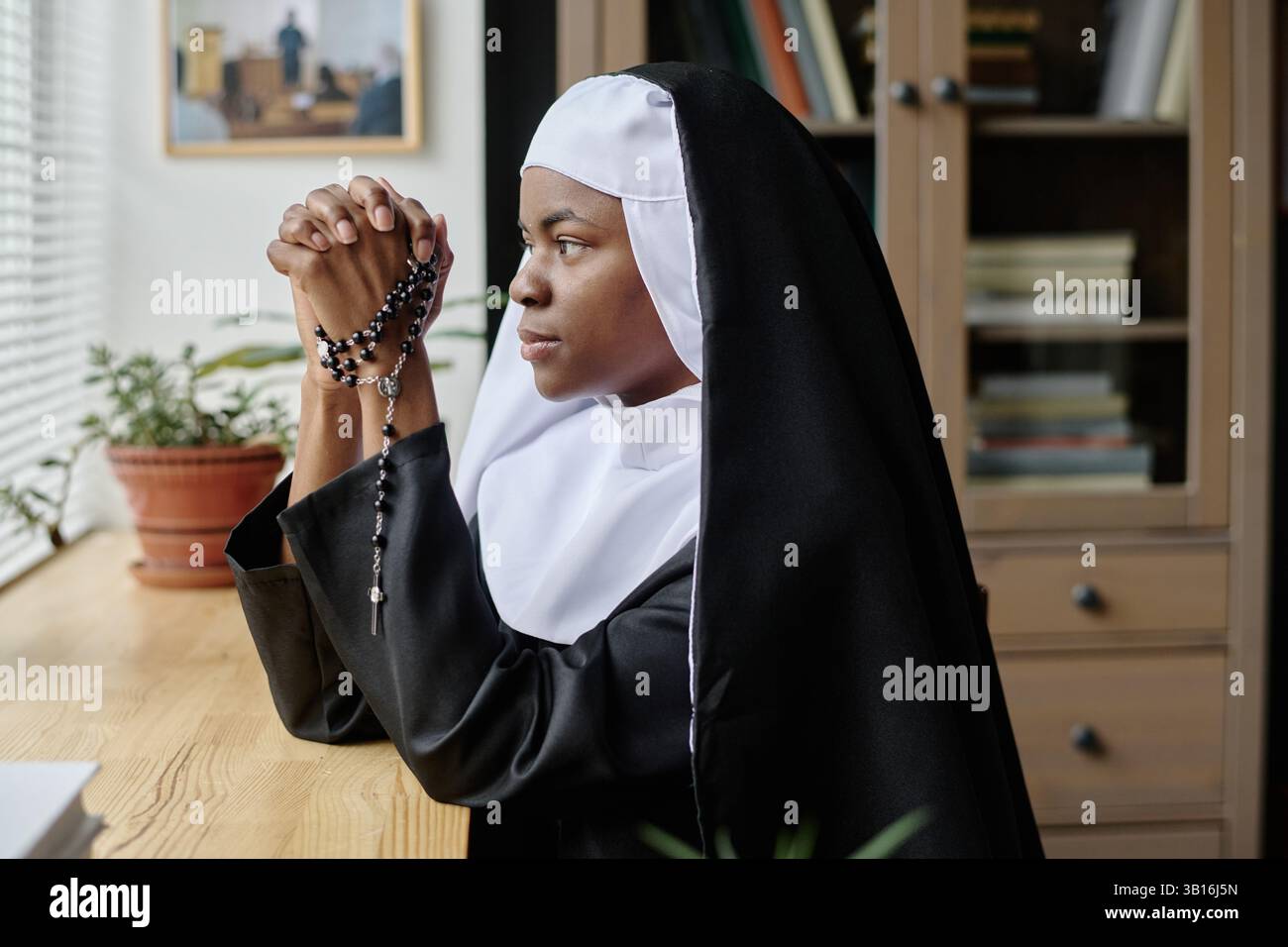 Medium shot of contemplative young African American nun leaning on ...