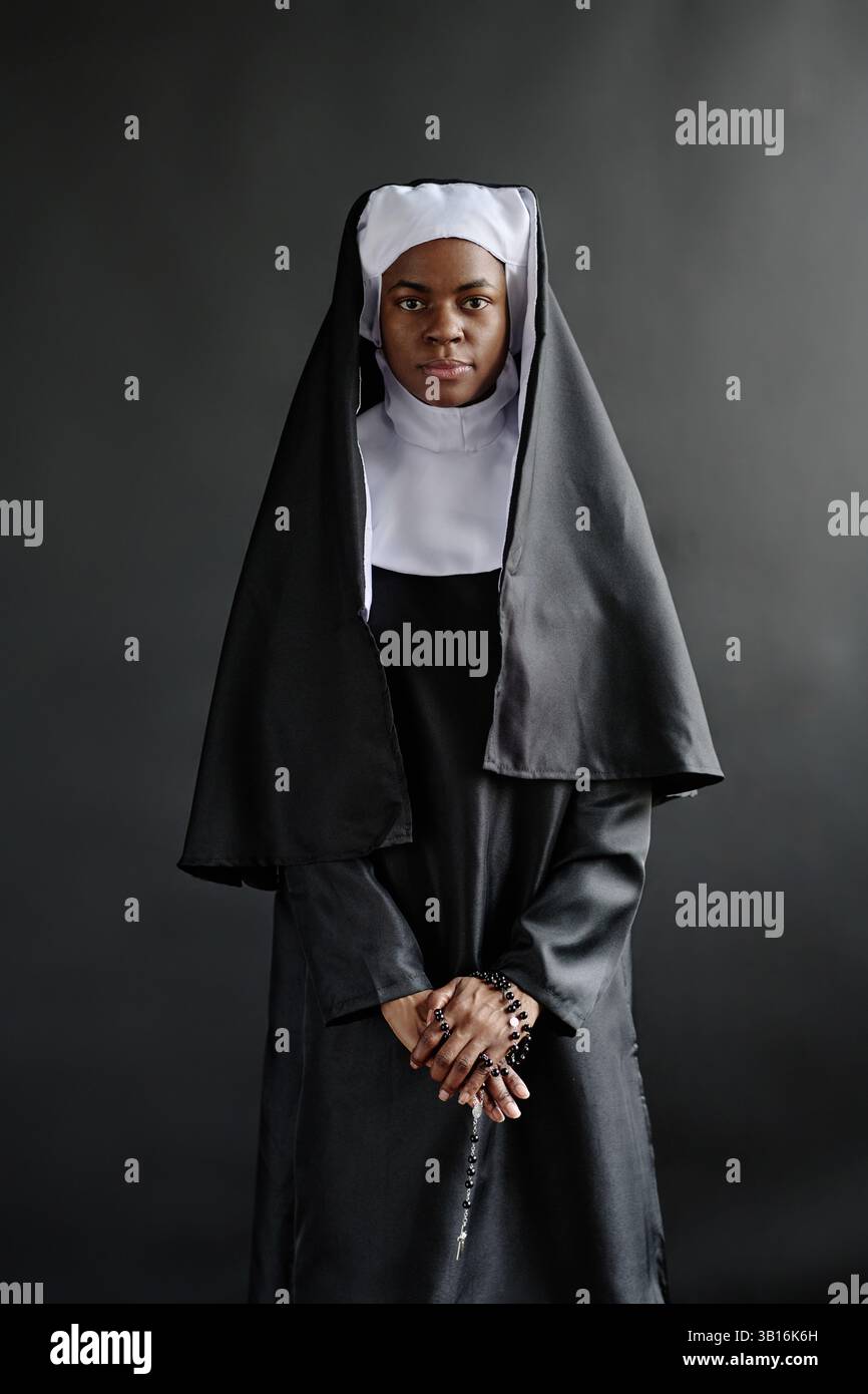 Vertical portrait of standing nun in black habit holding rosary and ...