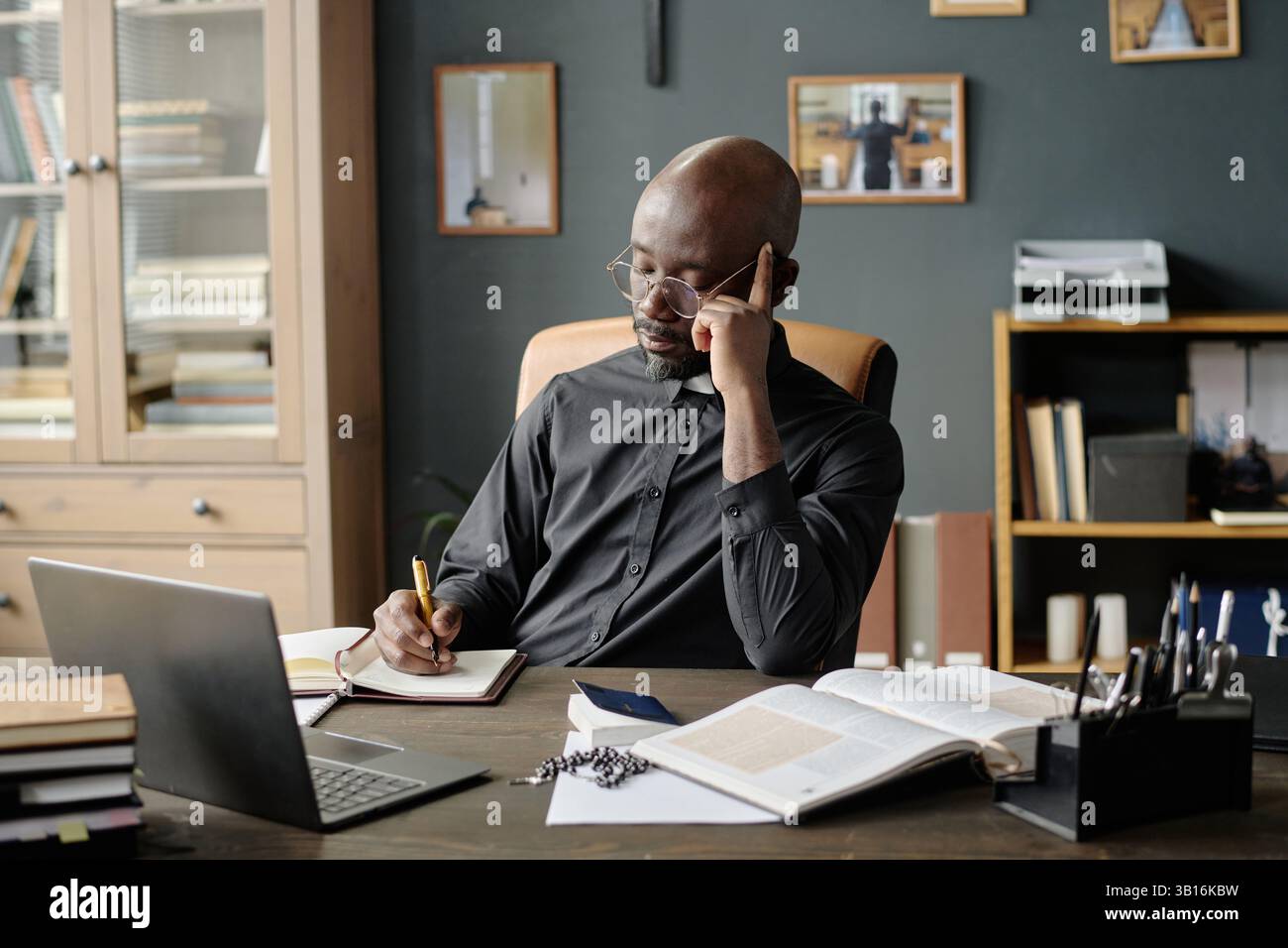 African American pastor leaning his head on hand writing on notebook ...