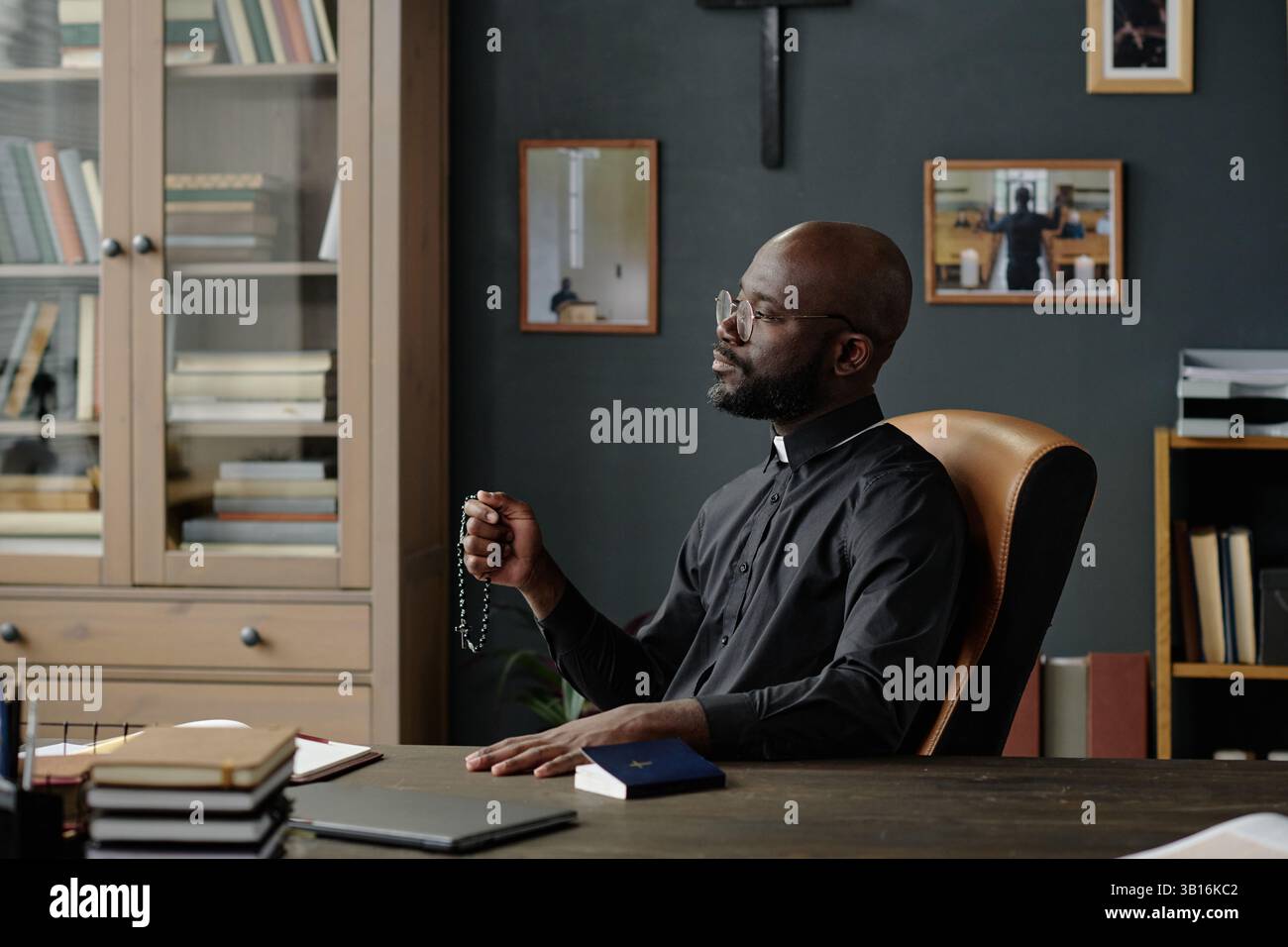 Handsome African American pastor holding rosary in hand while sitting ...