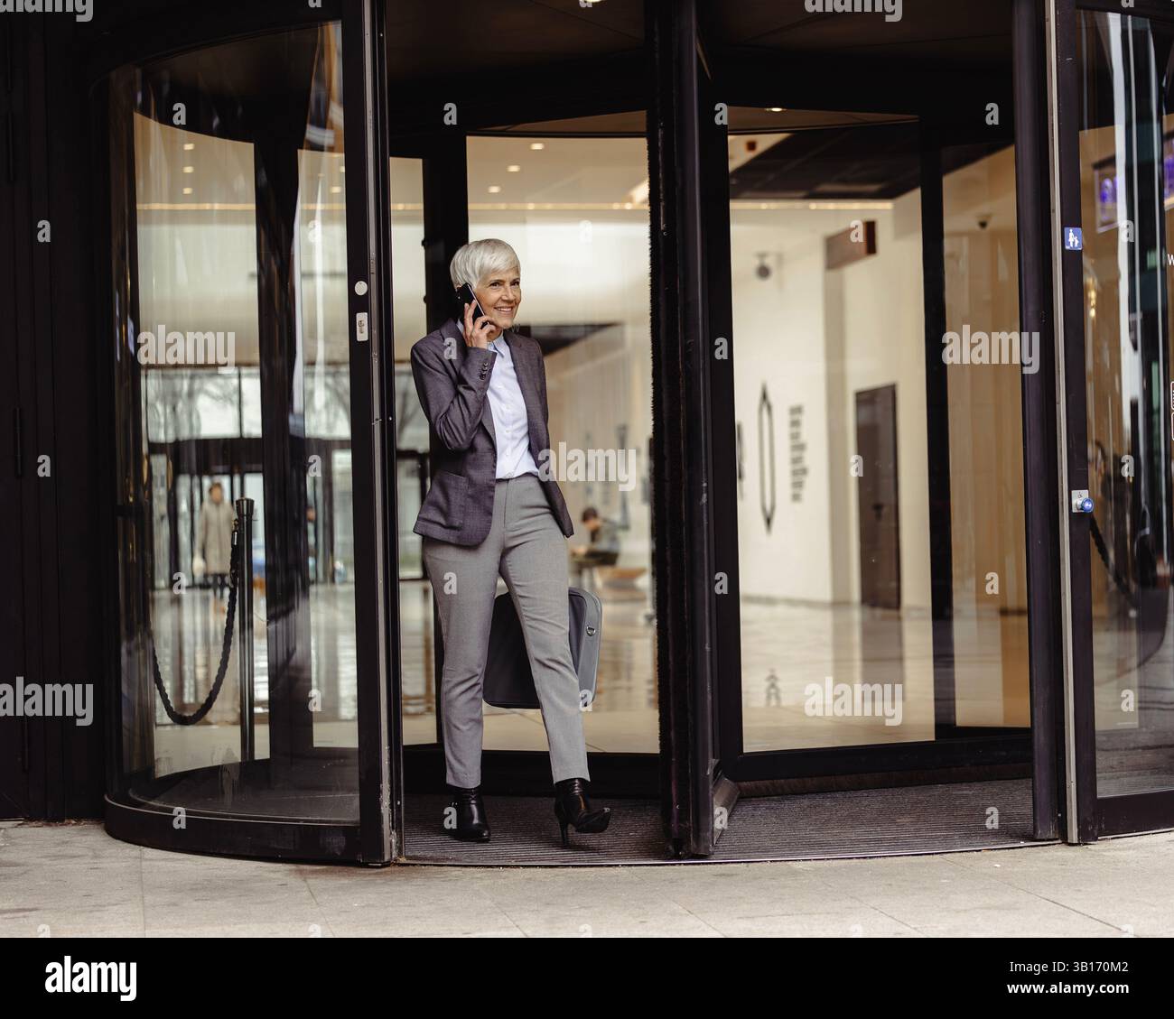 Senior business woman talking on smart phone while exiting office ...