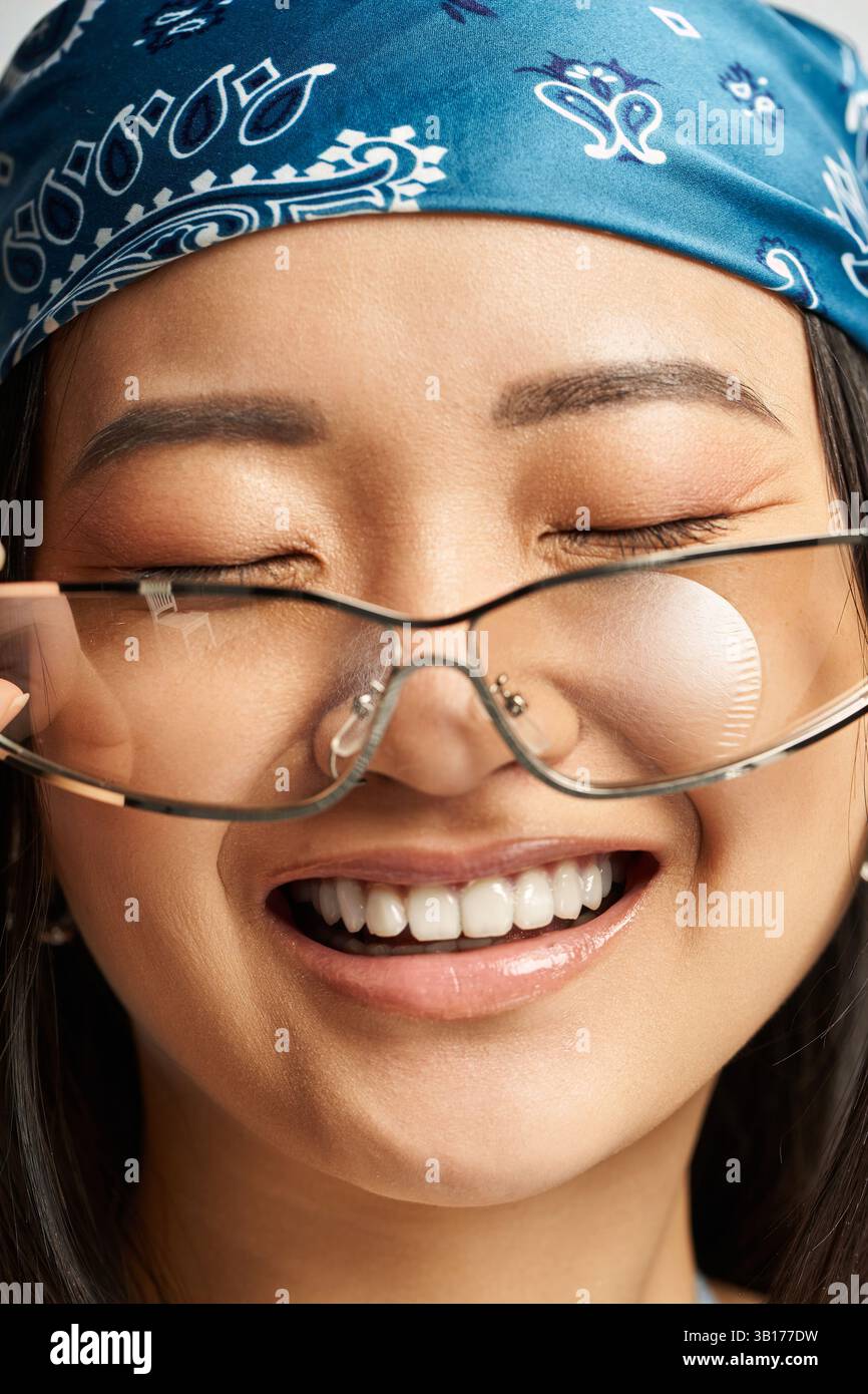 A joyful young woman, wearing glasses and a blue bandana, smiles ...