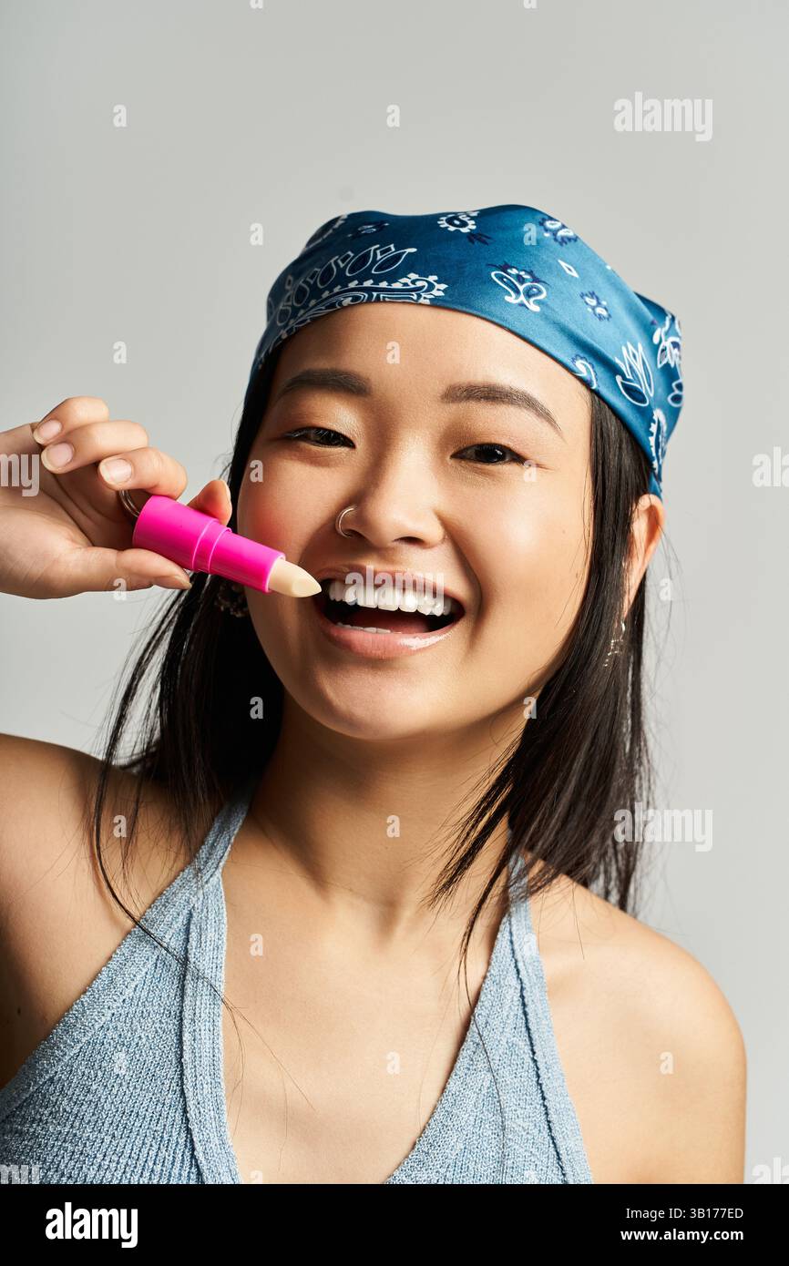 A young Asian woman joyfully holds bright makeup, smiling in a lively ...