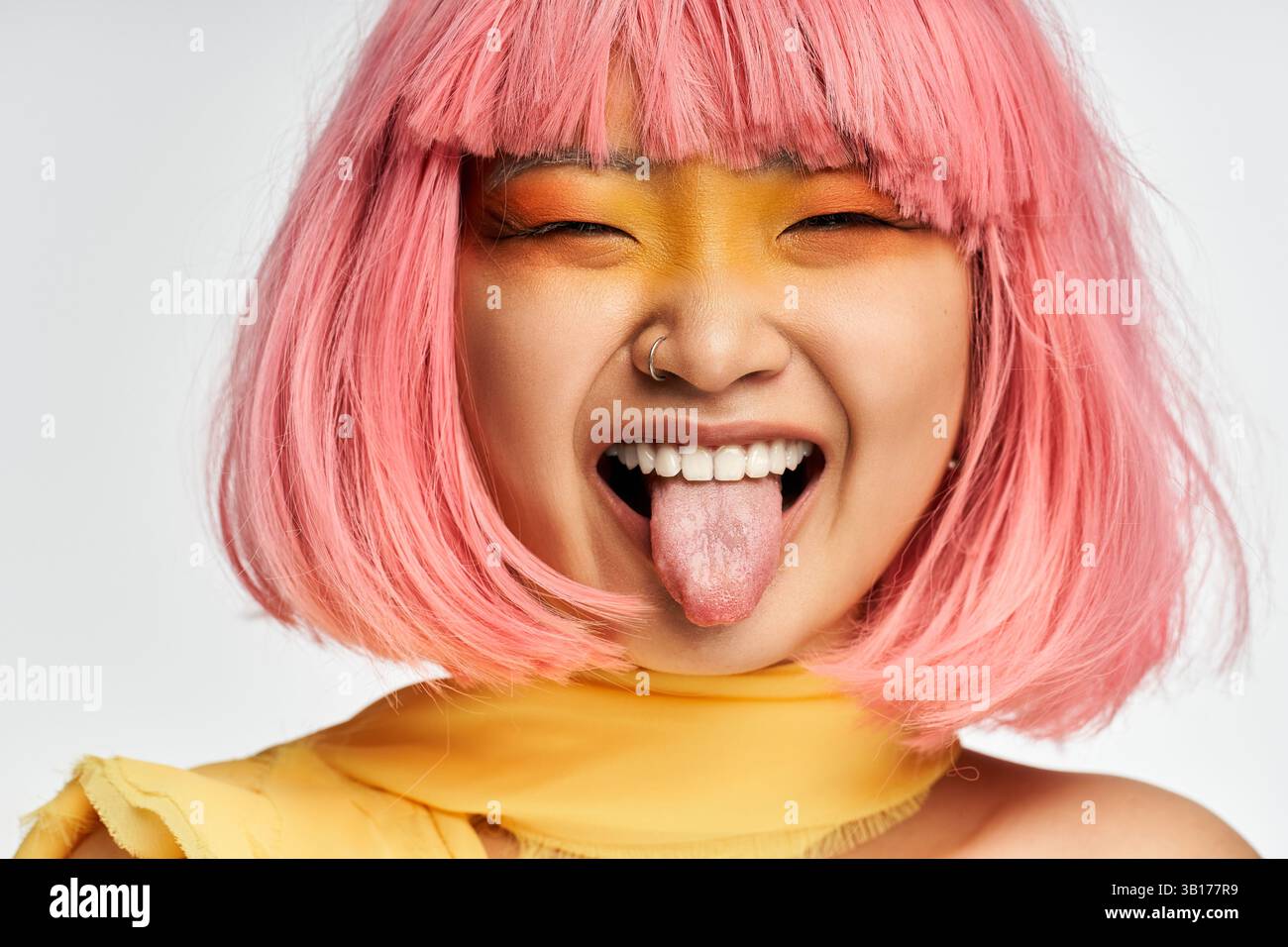 Joyful young woman with pink hair playfully sticks out her tongue ...