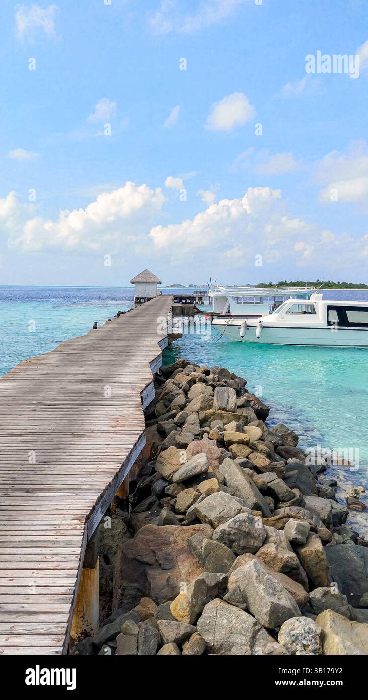 Wooden pier stretches over rocks and turquoise sea with boats docked ...