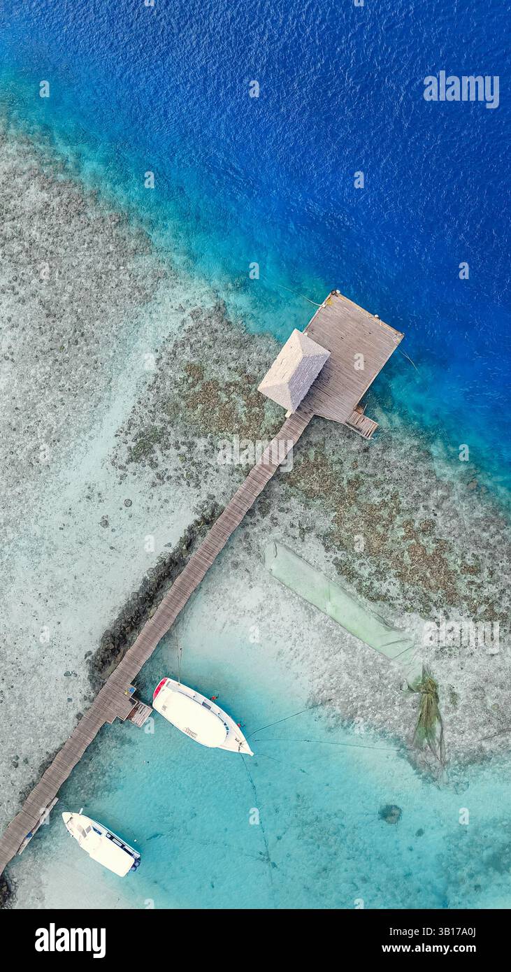 Wooden pier stretches over rocks and turquoise sea with boats docked ...