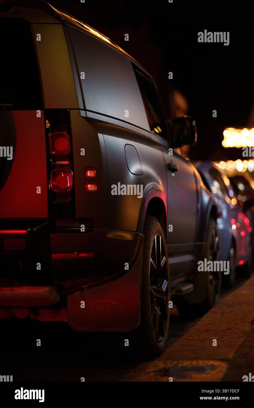 A matte gray Land Rover Defender parked on a city street at night, tail ...