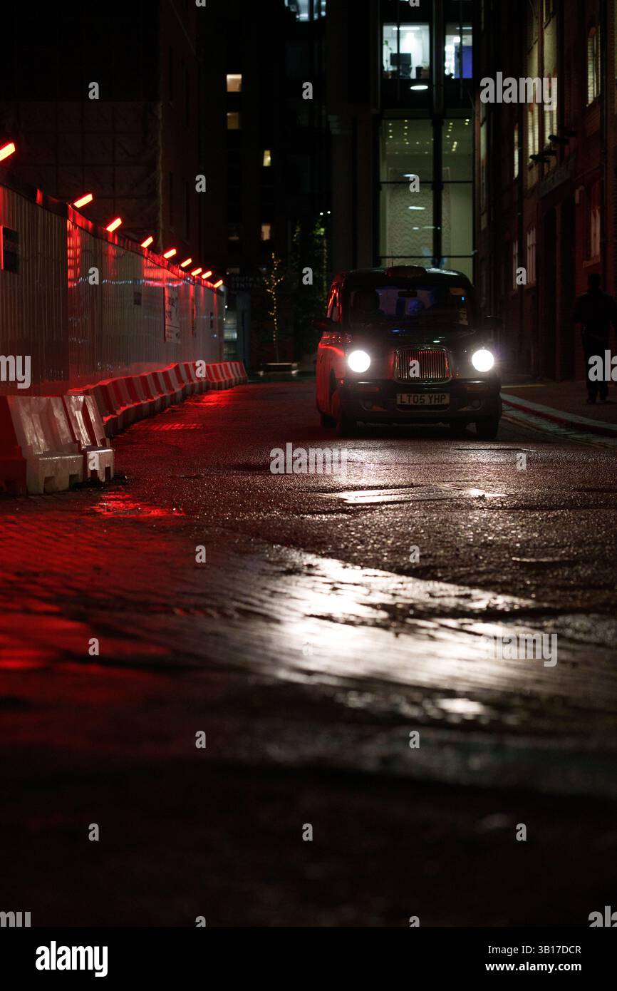 A London black cab drives down a narrow city street at night ...