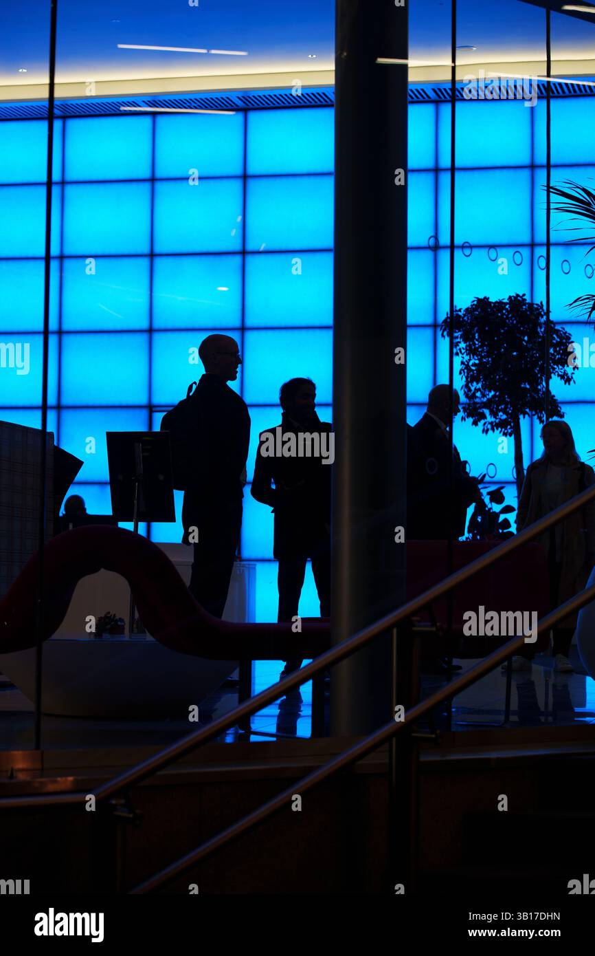 Silhouetted figures stand in a modern, blue-lit atrium, creating a ...