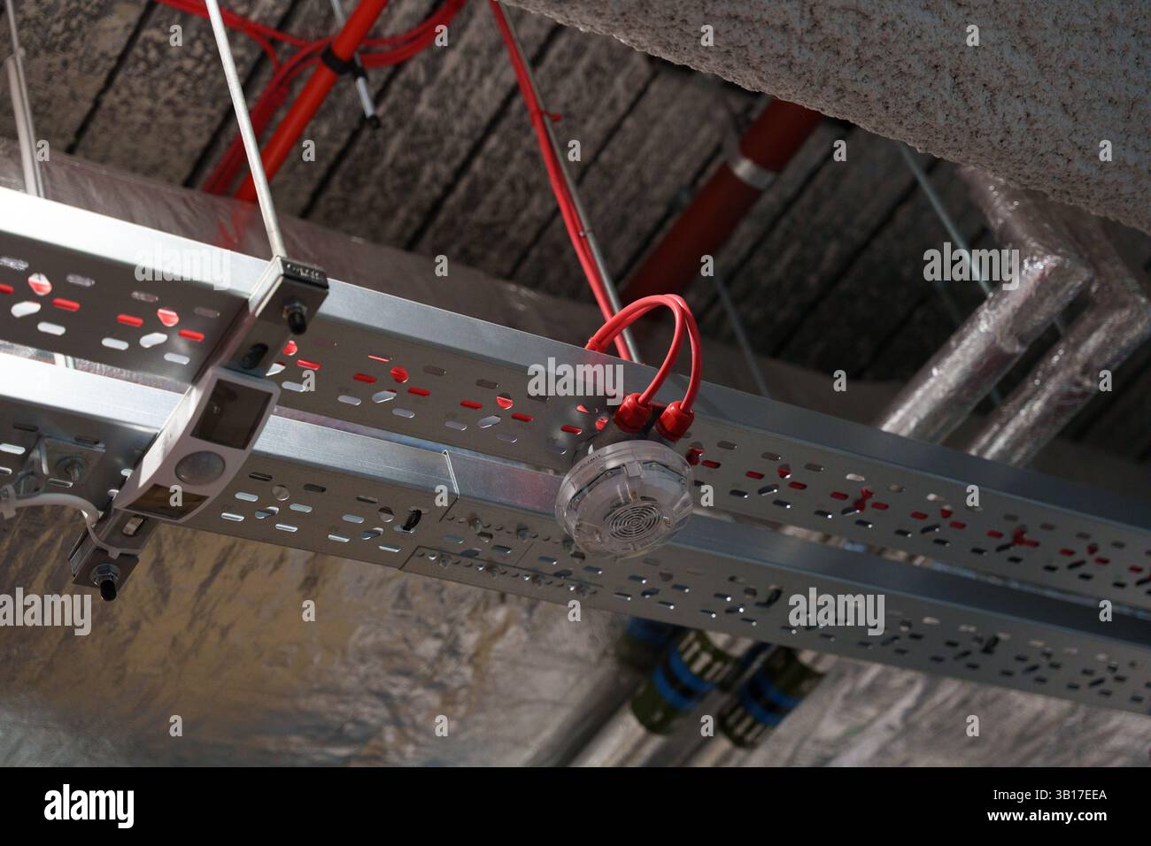 A fire alarm sensor with red wires is attached to metal cable trays ...
