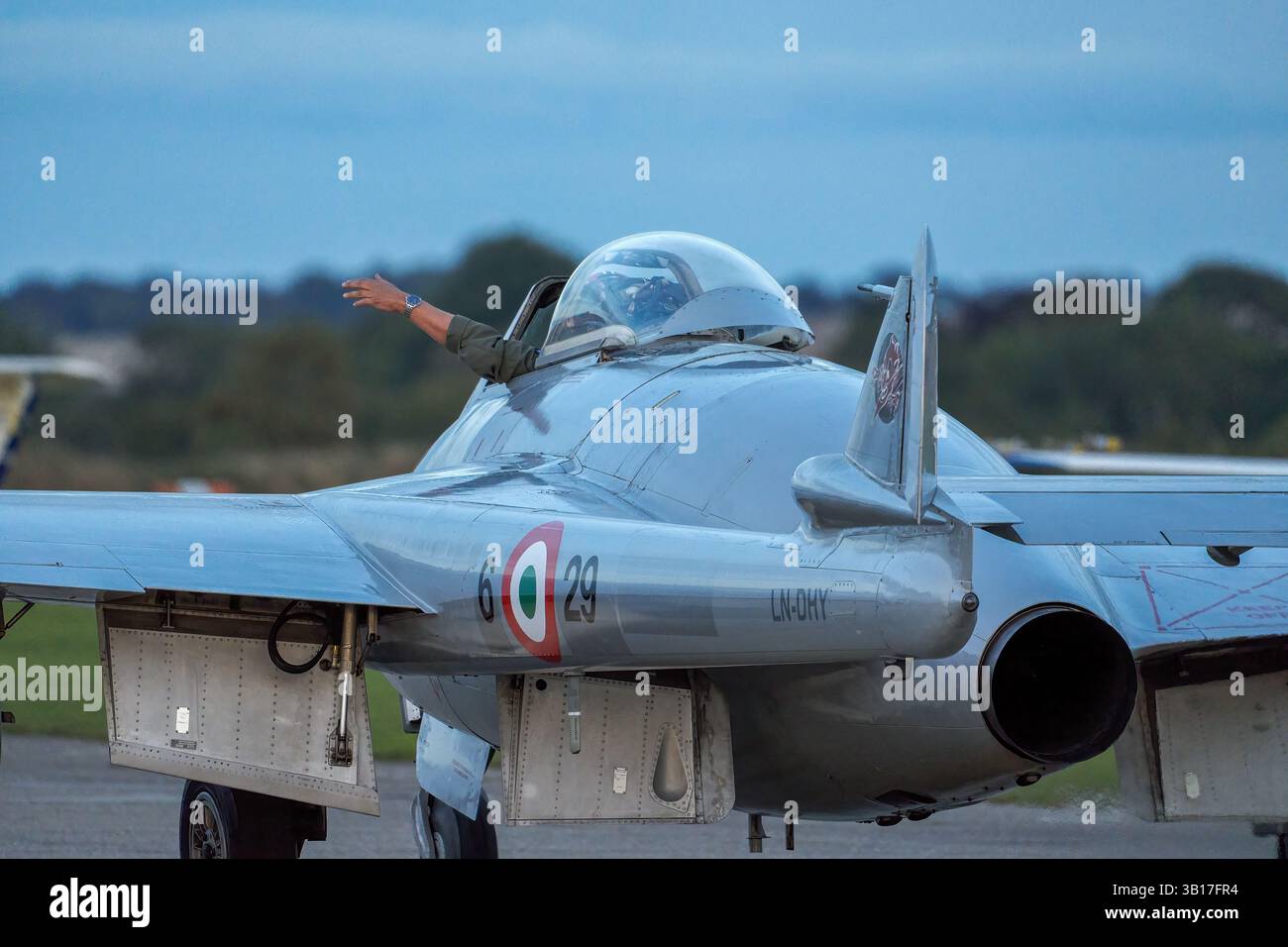 A silver De Havilland Vampire FB.53 fighter jet taxis on a runway at dusk in Duxford, England ...