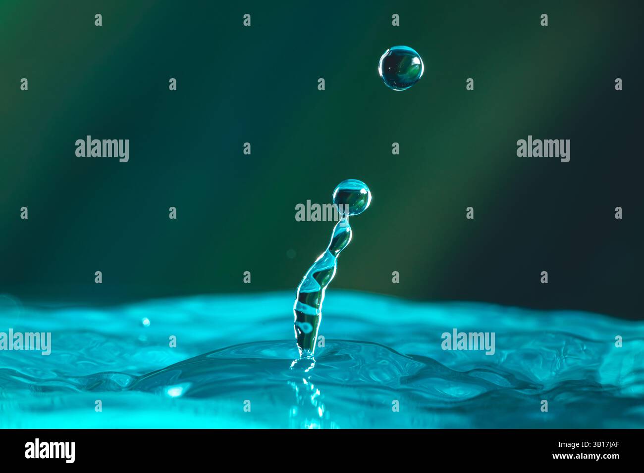 Water droplets fall down closely into the dark blue water, making it ...