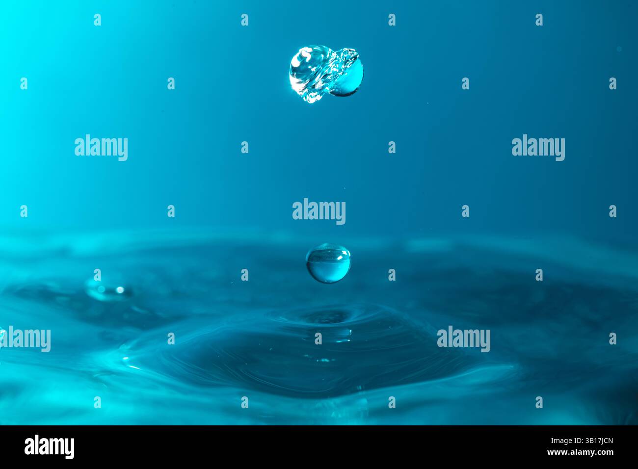 Water droplets fall down closely into the blue water, making it the ...