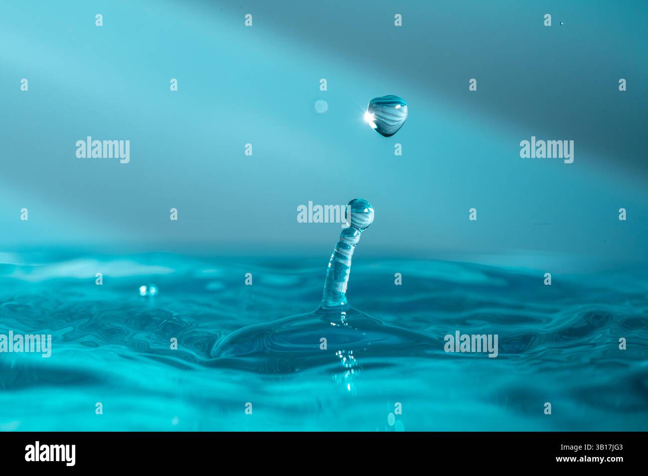 Water droplets fall down closely into the blue water, making it the ...