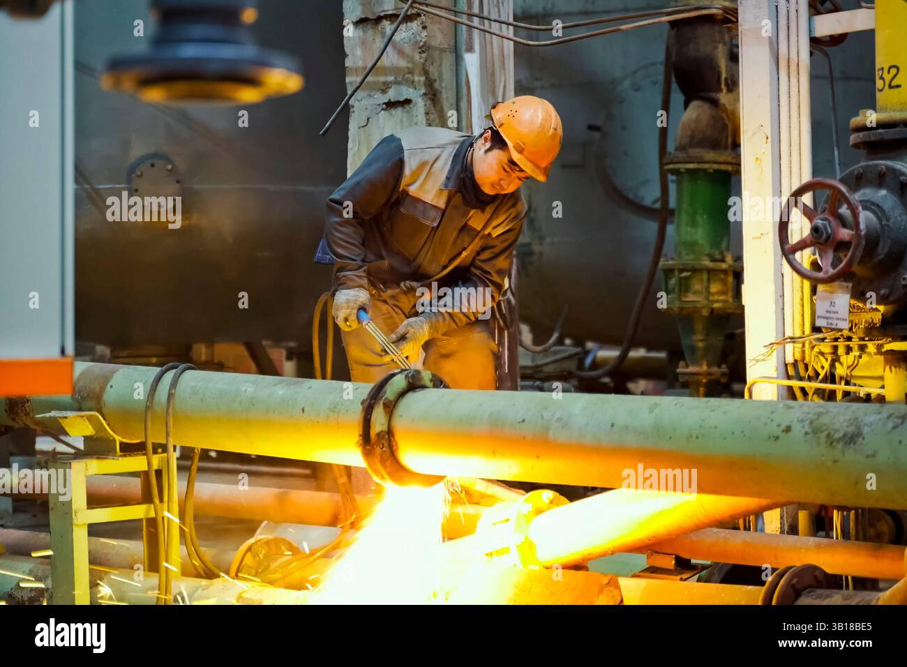 A welder welds a pipeline. Installation of pipelines at an oil refinery ...