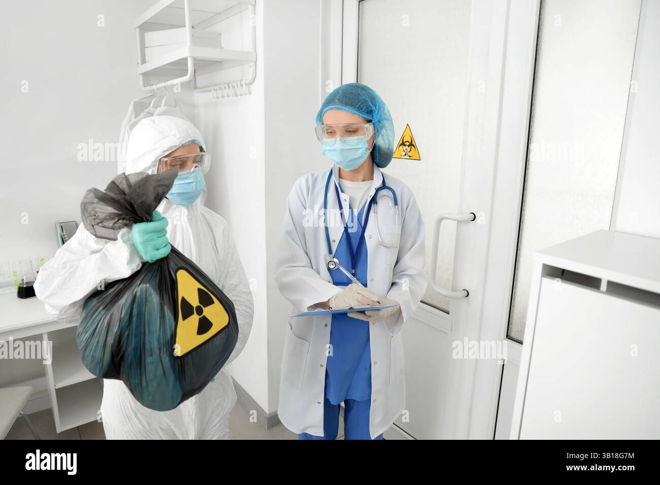 Workers in protective uniforms and with bag of radioactive waste in ...