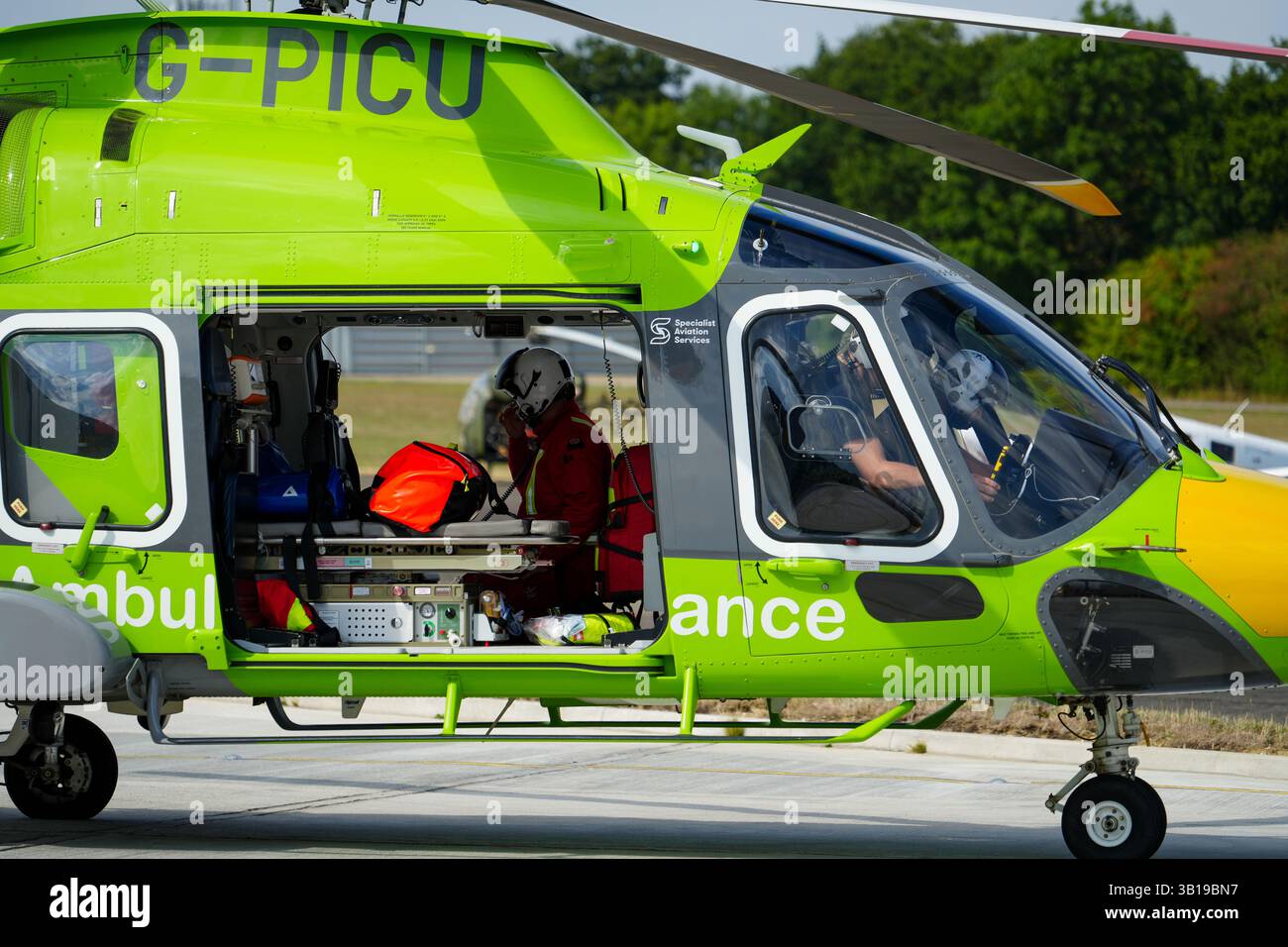 A bright green and yellow air ambulance helicopter, G-PICU, stands ...
