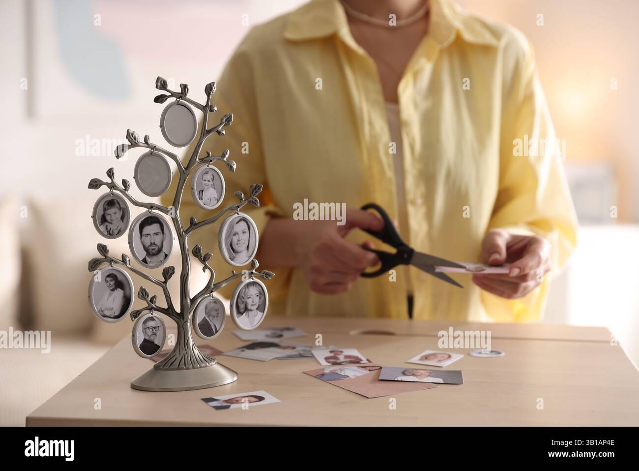 Woman cutting out pictures of her relatives at table indoors, focus on ...