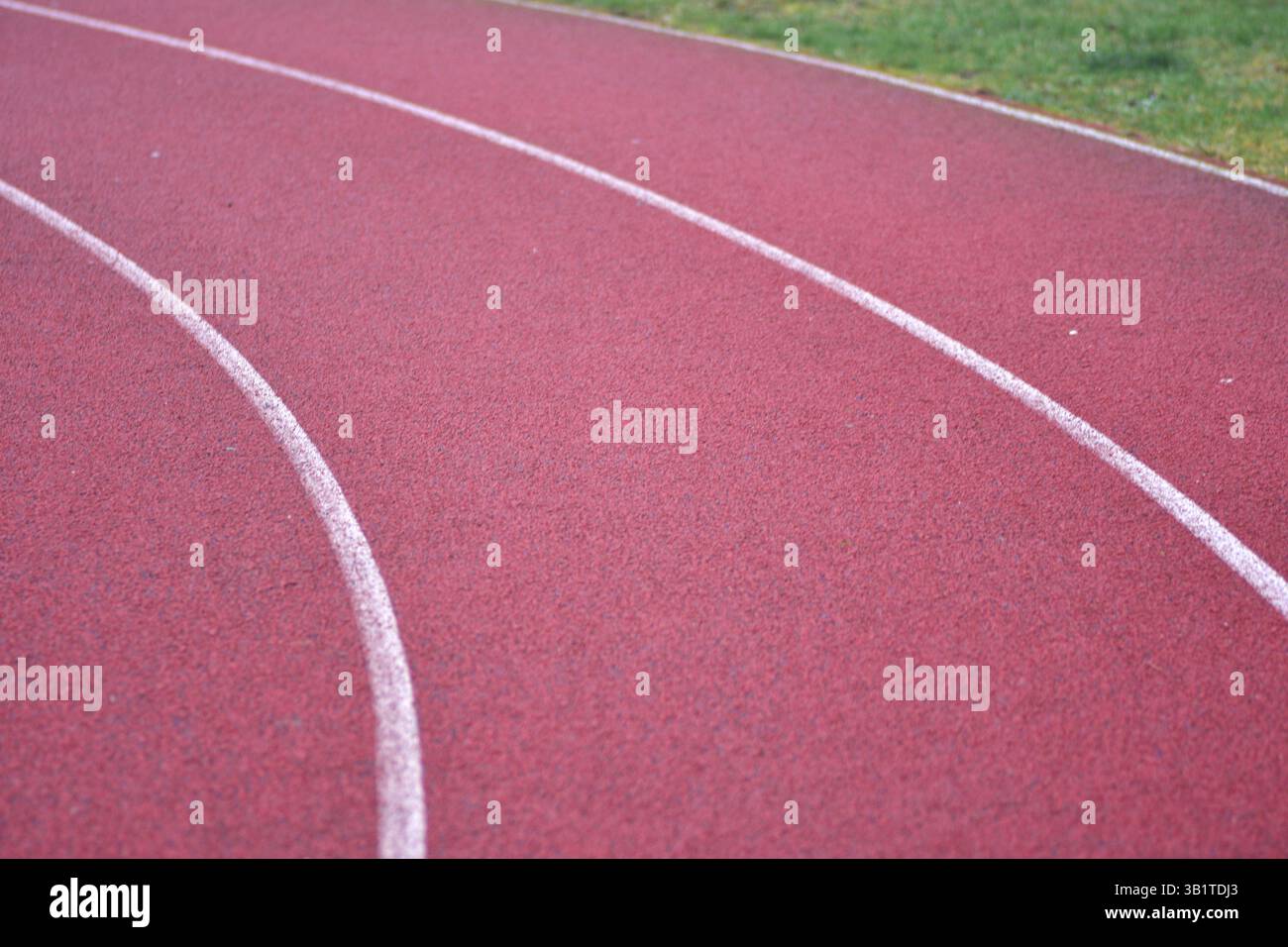 red running track curve with white lines and green grass in right side ...