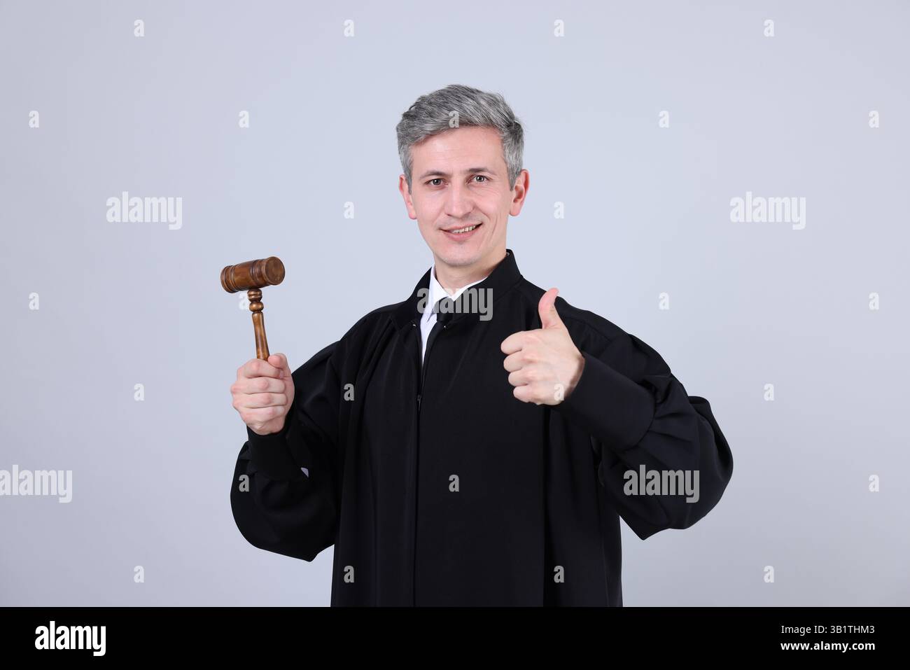 Smiling judge with mallet showing thumbs up on grey background Stock ...