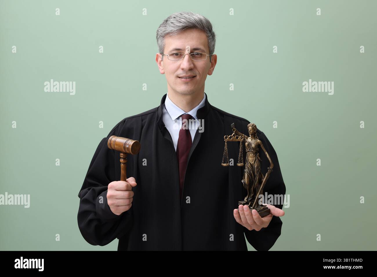 Smiling judge with mallet and statue of Lady Justice on green ...