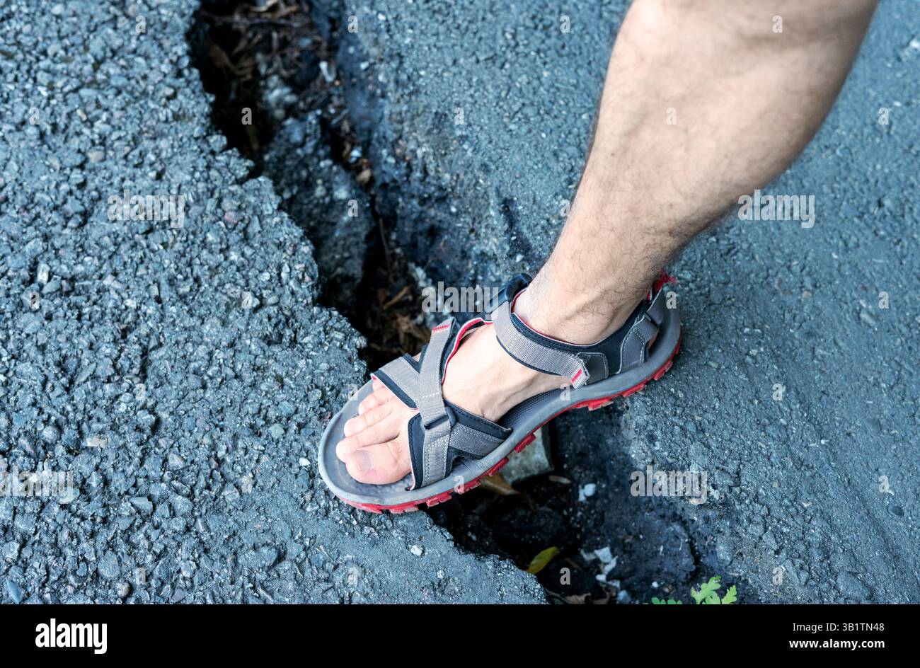 Foot in a grey sandal steps into crack on an asphalt road ...