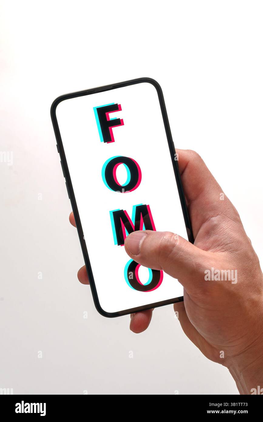 Hand holding a smartphone displaying the word FOMO (Fear of missing out ...
