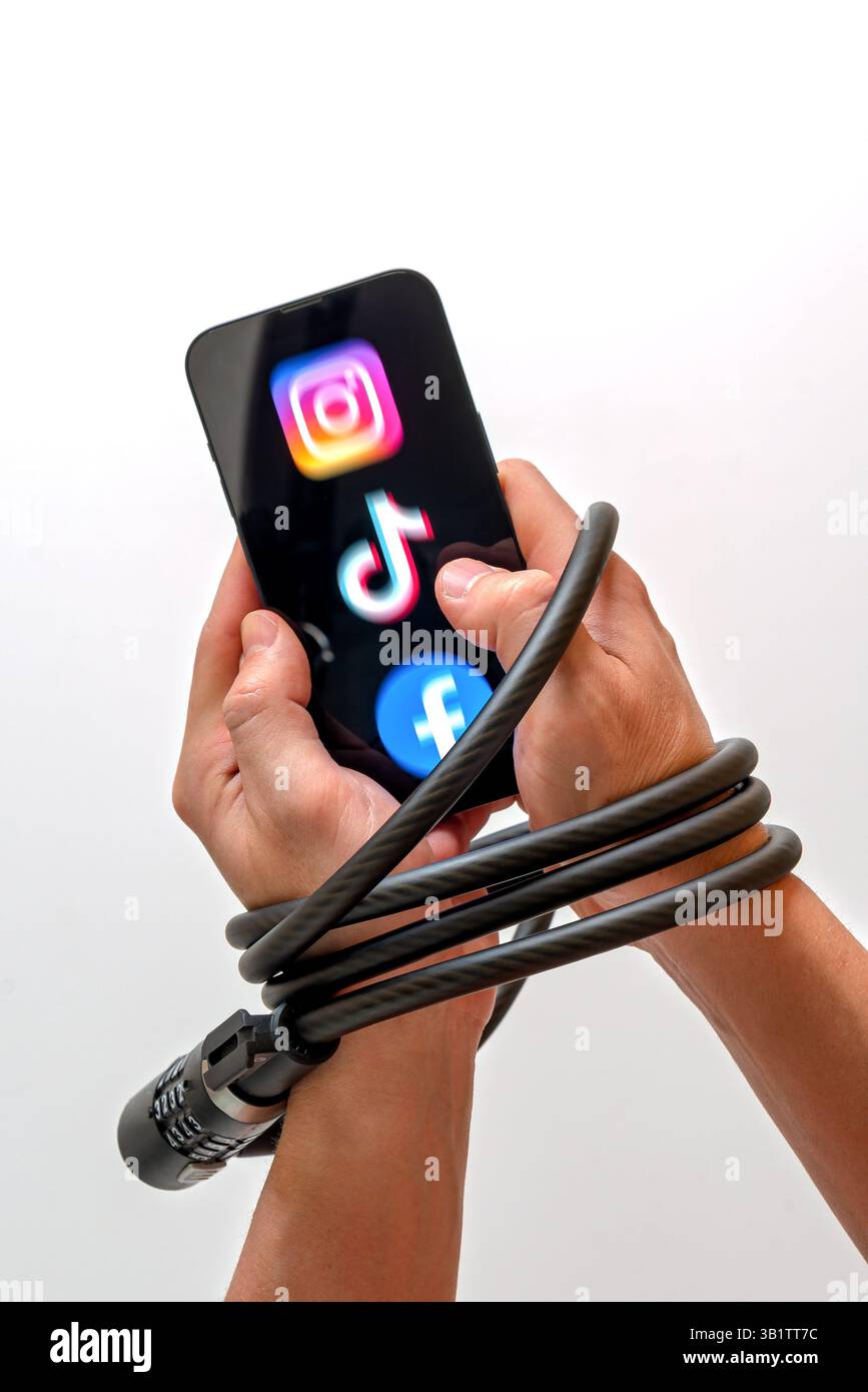 Hands are clamped with a cable lock, holding a smartphone with logos ...