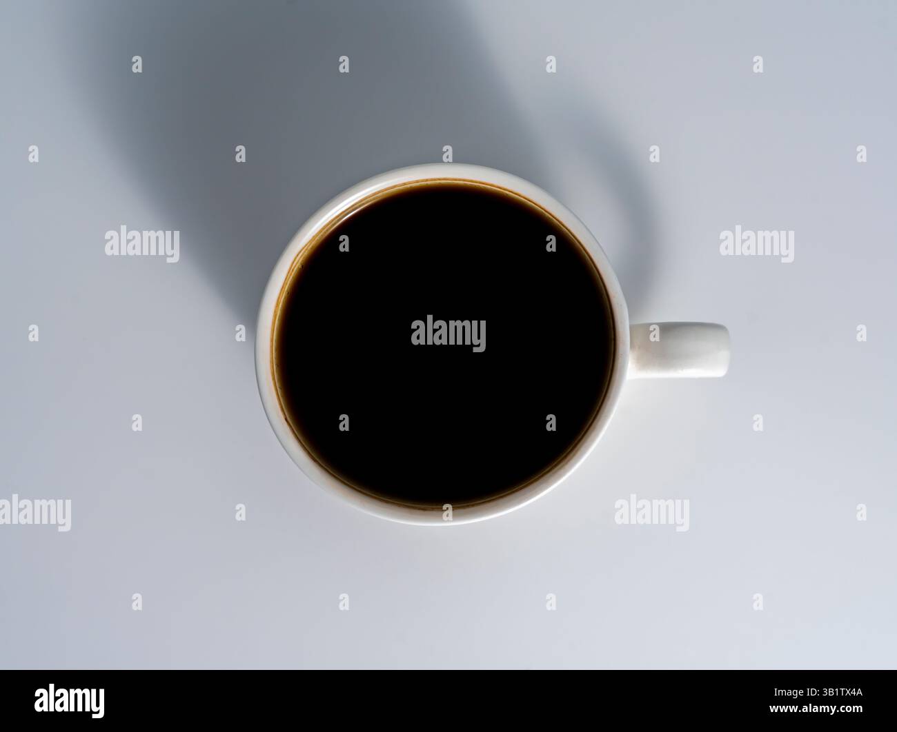 Overhead image of a full white ceramic cup with black coffee casting a ...