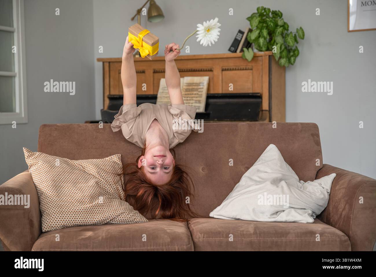 Redhead child hanging upside down on a brown sofa in the living room ...