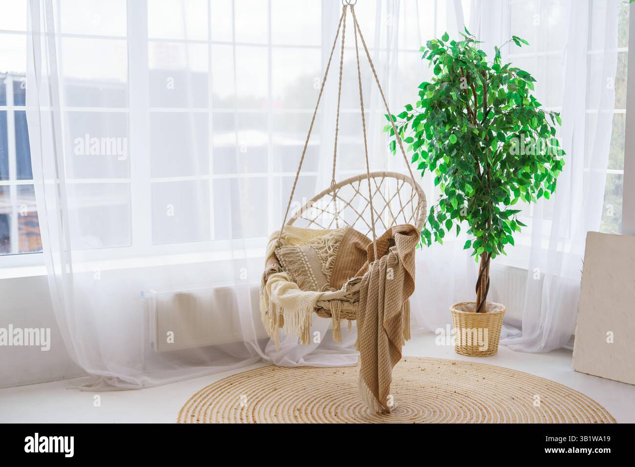 Cozy hanging wicker chair with soft beige plaid in living room with ...