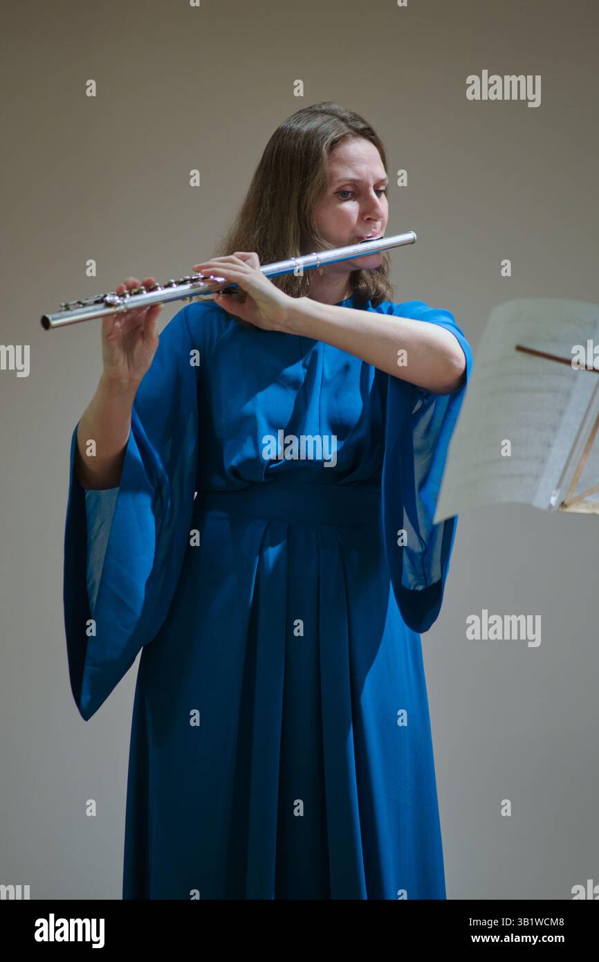 Female musician in a blue dress plays the flute while reading sheet ...