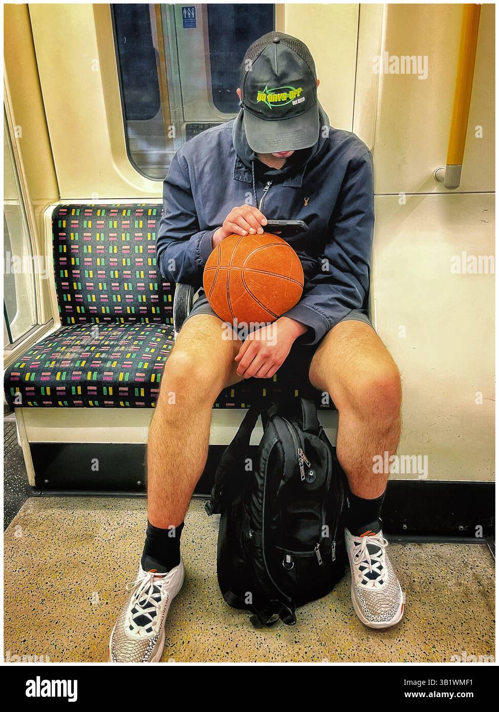 Man in baseball cap holding a basketball whilst sitting on a London ...
