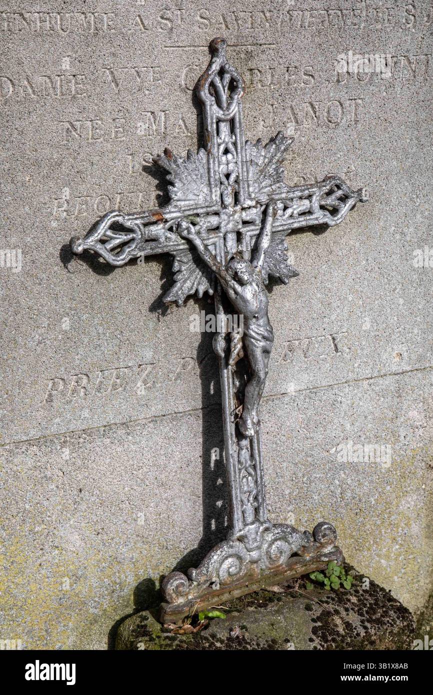 Metal Jesus figure on the cross leaning against gravestone in Montmartre Cemetery in Paris ...