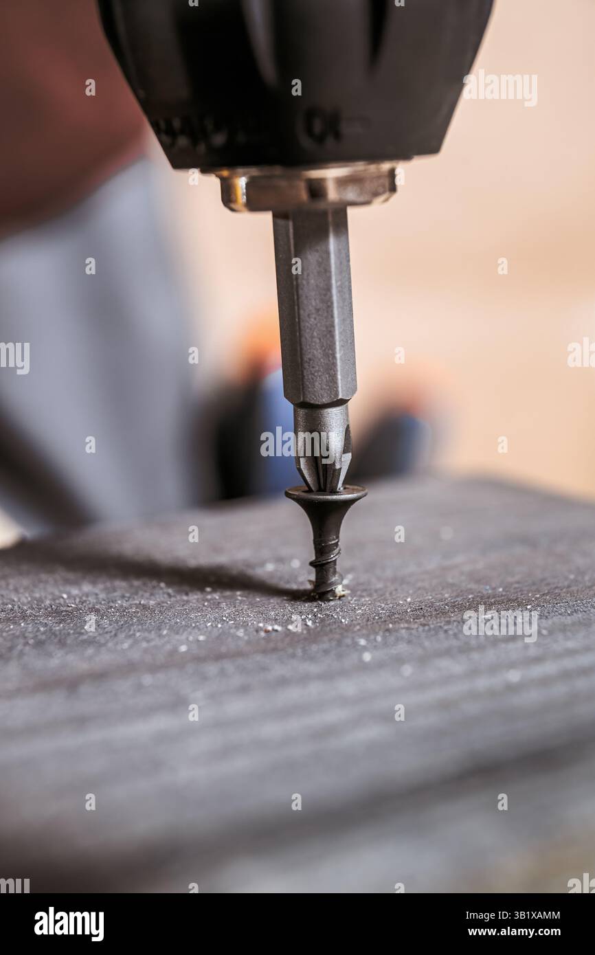 A drill bit presses a black screw down into wood with visible pressure ...