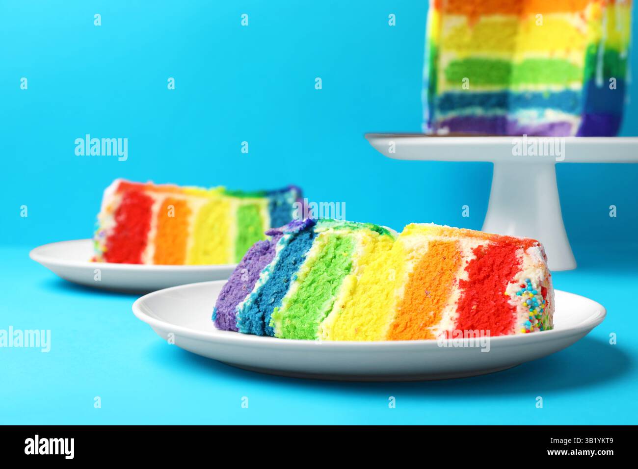 Pieces of delicious rainbow cake on light blue table, closeup Stock ...