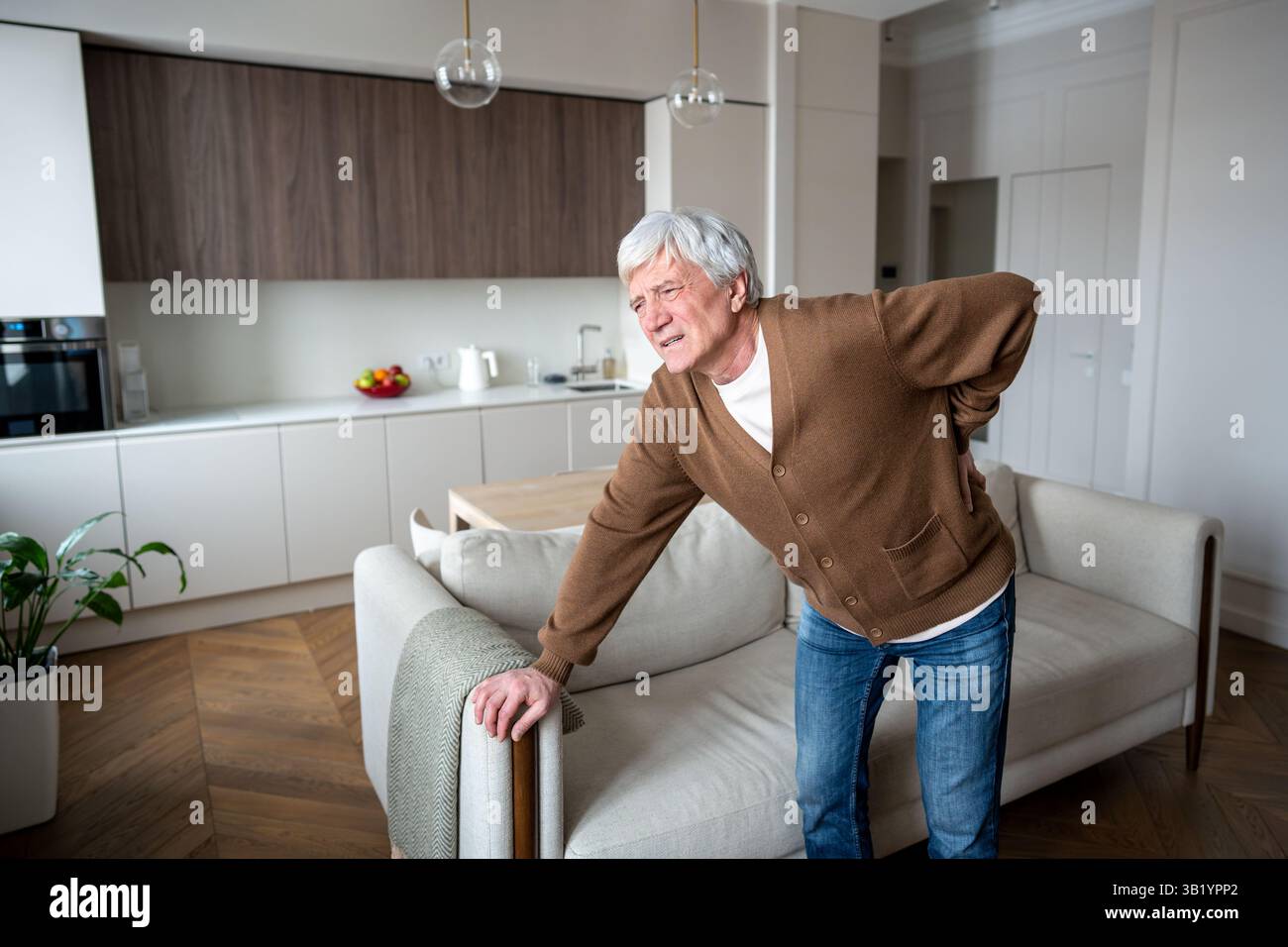 Back pain. Unhappy elderly man hunched in pain grips injured lower back ...