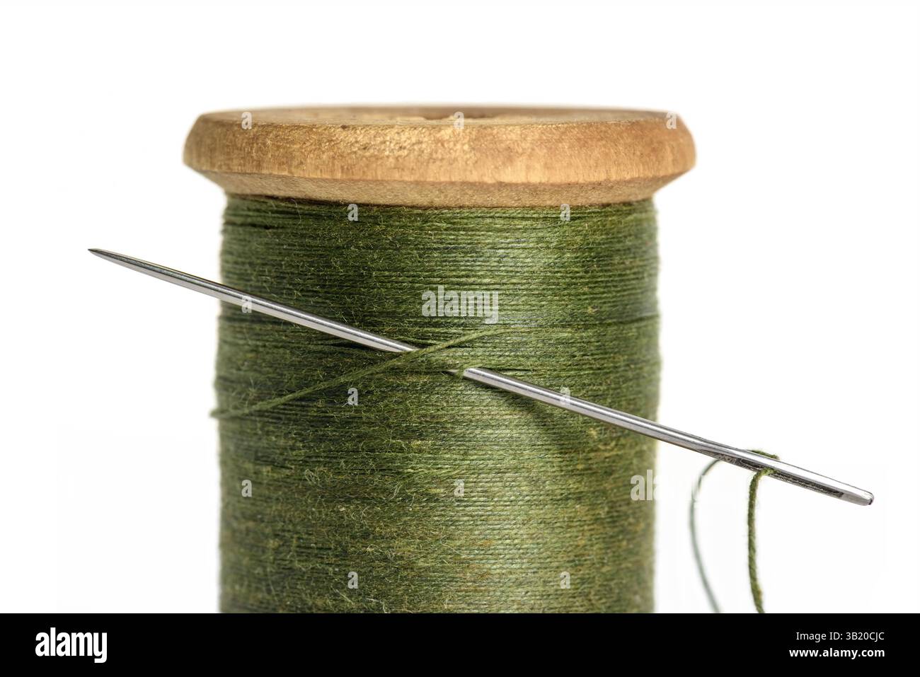 Old Single wooden spool of thread olive green color and needle closeup ...