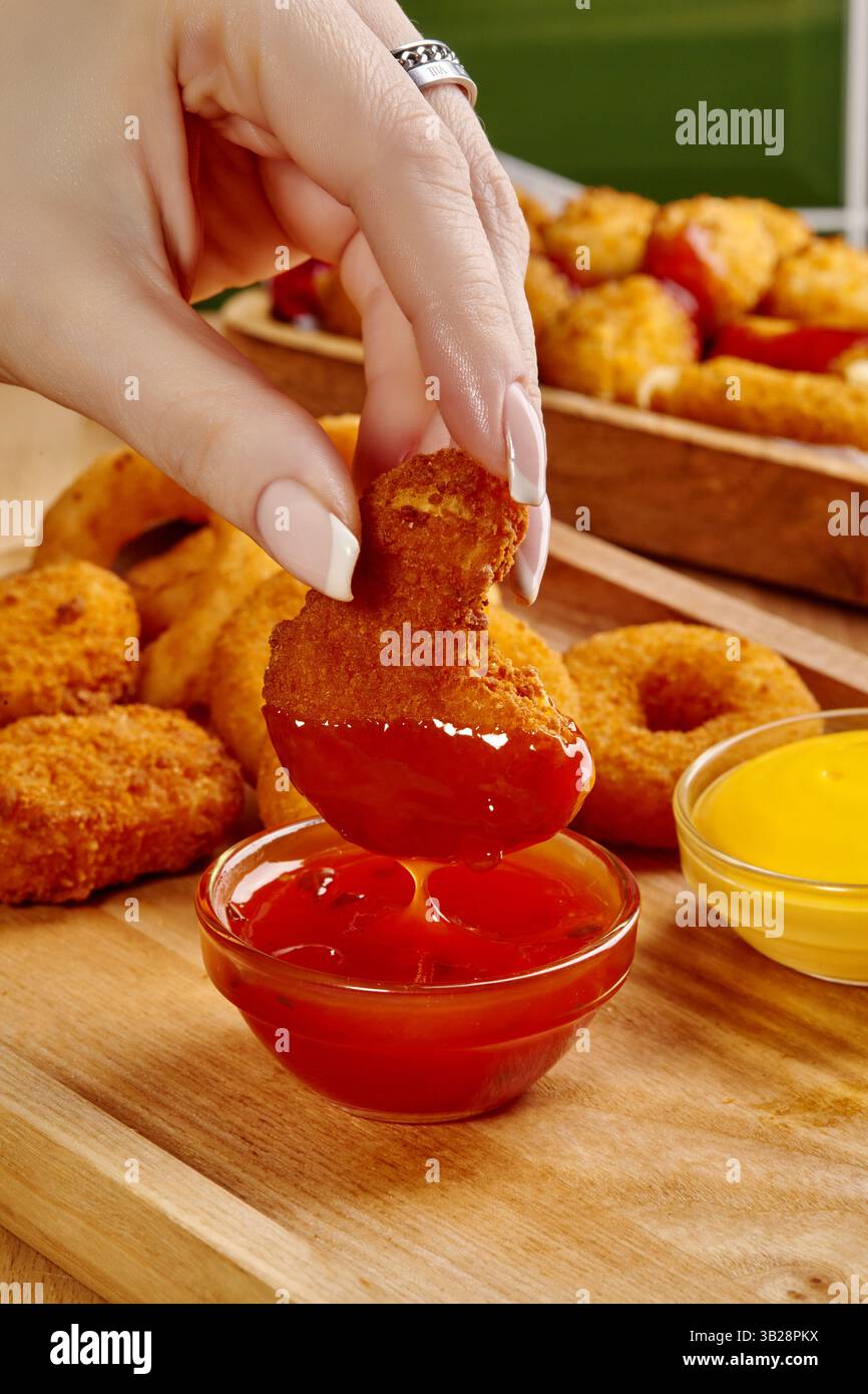 Woman dipping a breaded chicken nugget into red sauce, enjoying a ...